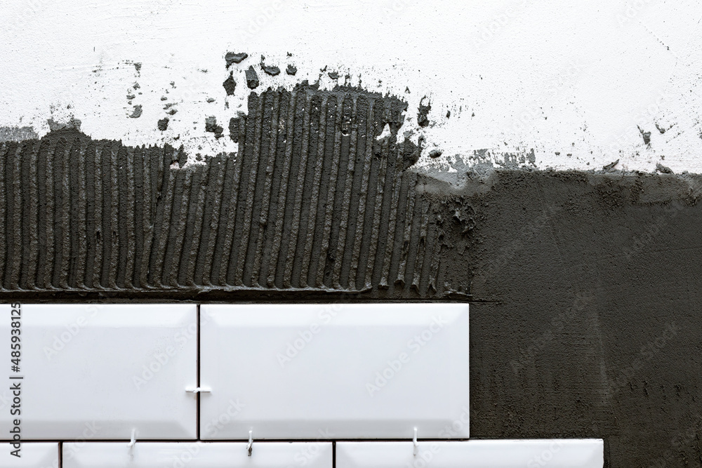 Wall cladding. White glazed ceramic tiles with tile spacer and glue on ...