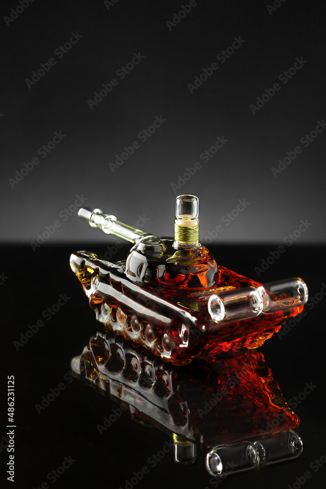 glass bottle made in the form of a tank stands on a mirror surface on a ...