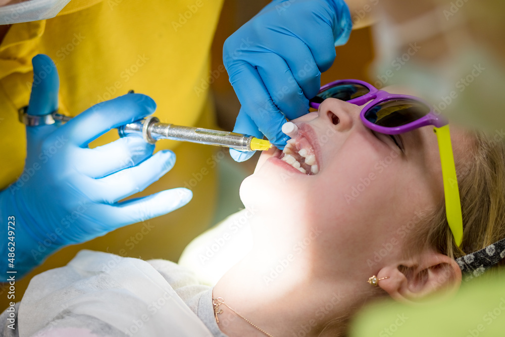side view of dentist holding a syringe and anesthetizing her little ...