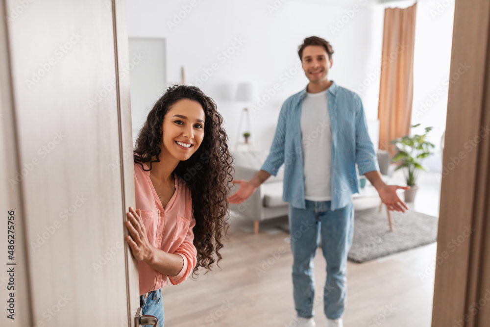 Foto de Happy young couple inviting people to enter their apartment do ...
