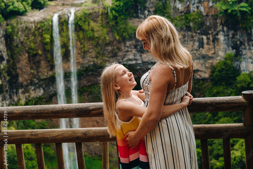 Mom and daughter are hugging each other near a waterfall in Chamarel ...