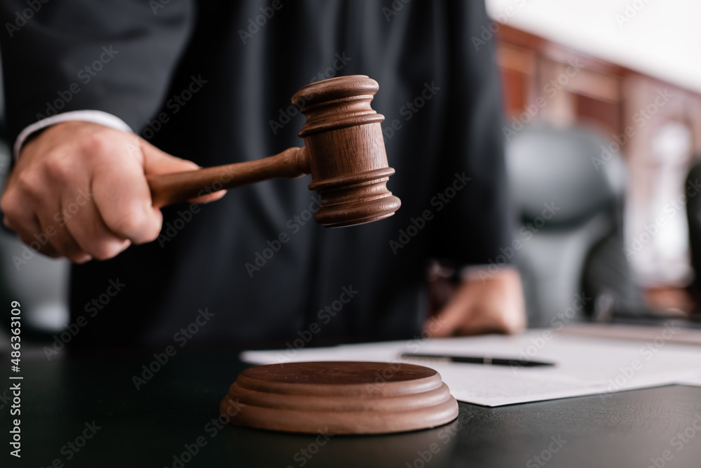partial view of blurred judge holding gavel during sentencing in court ...