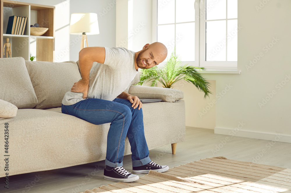 Unhealthy young man sit on couch at home struggle with backache. Pain ...