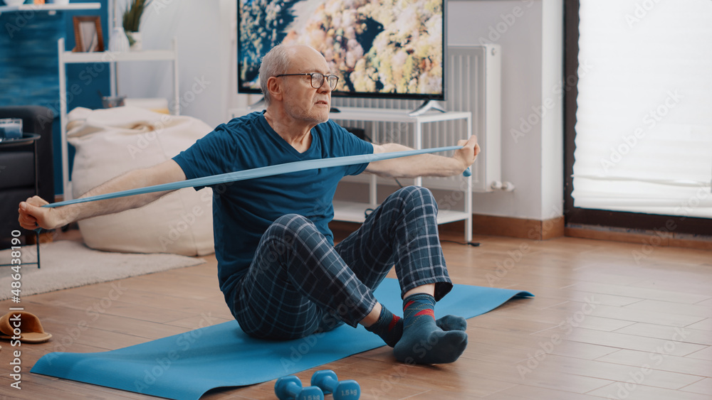 Retired adult pulling resistance band and sitting on yoga mat at home ...