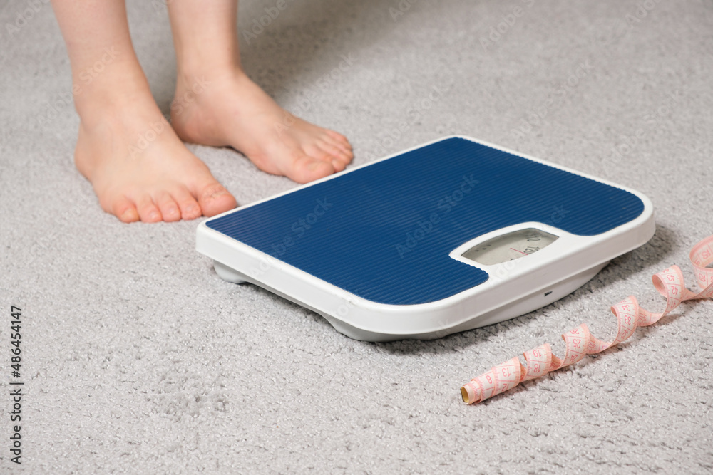 Bare feet and a floor blue scale with a measuring centimeter tape, the ...