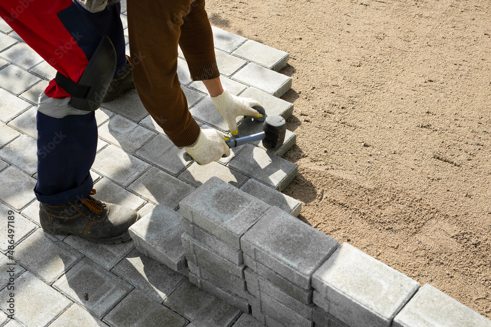 Hands of a worker installing concrete blocks, paving slabs with a ...