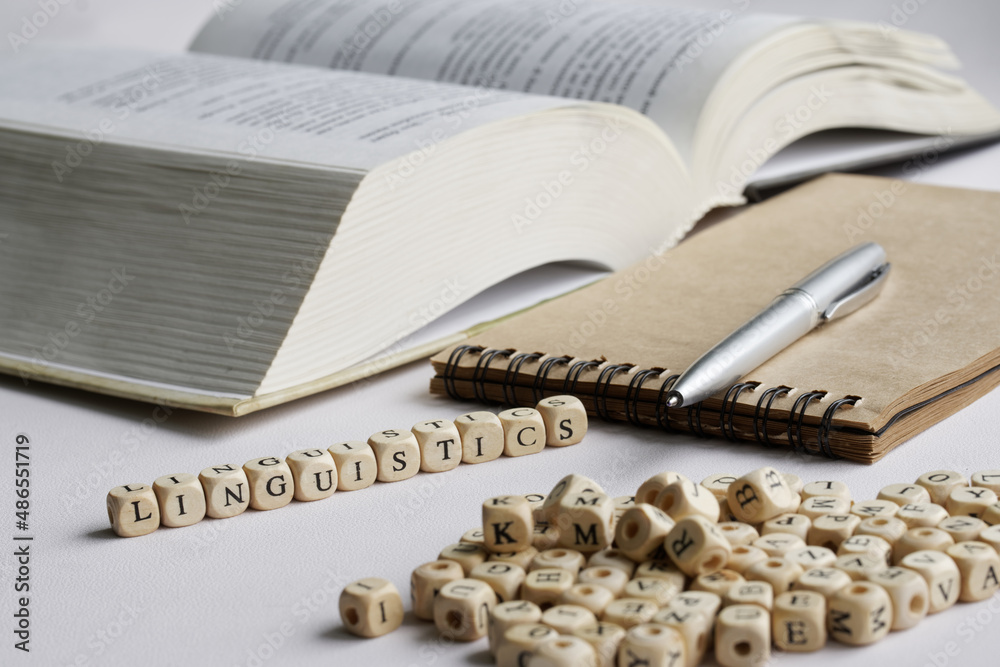 Word linguistics next to notebook, pen, open book and many letters ...