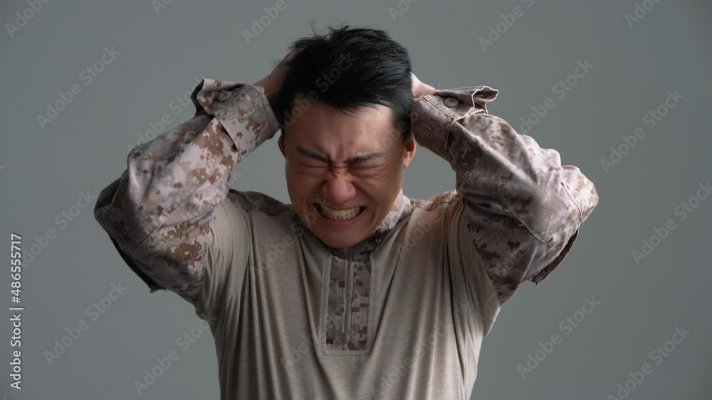 Angry soldier Asian man screaming at the camera in the grey studio ...