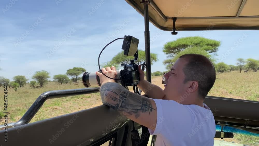 A tourist with a large camera takes pictures of animals from a safari ...