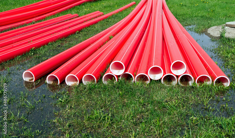 Bright red plastic water pipes on a wet green lawn are prepared for the ...