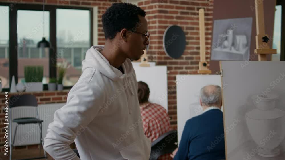 Male teacher looking at elder student drawing on canvas, explaining ...