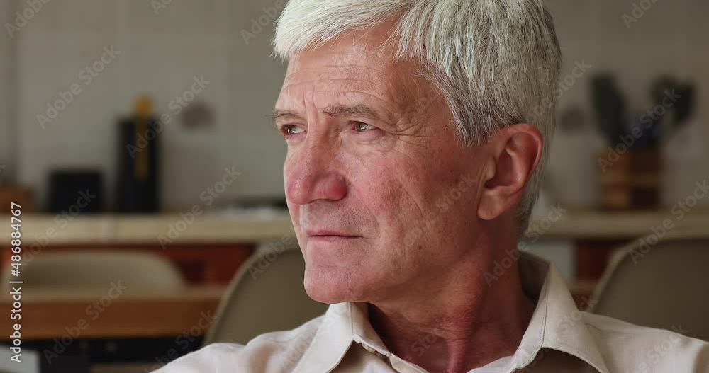 Close up face serious grey-haired man sit indoor staring into distance ...