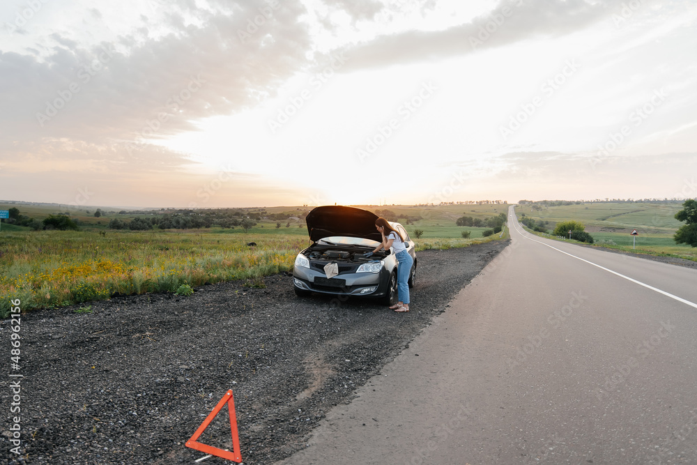 A young girl stands near a broken car in the middle of the highway ...