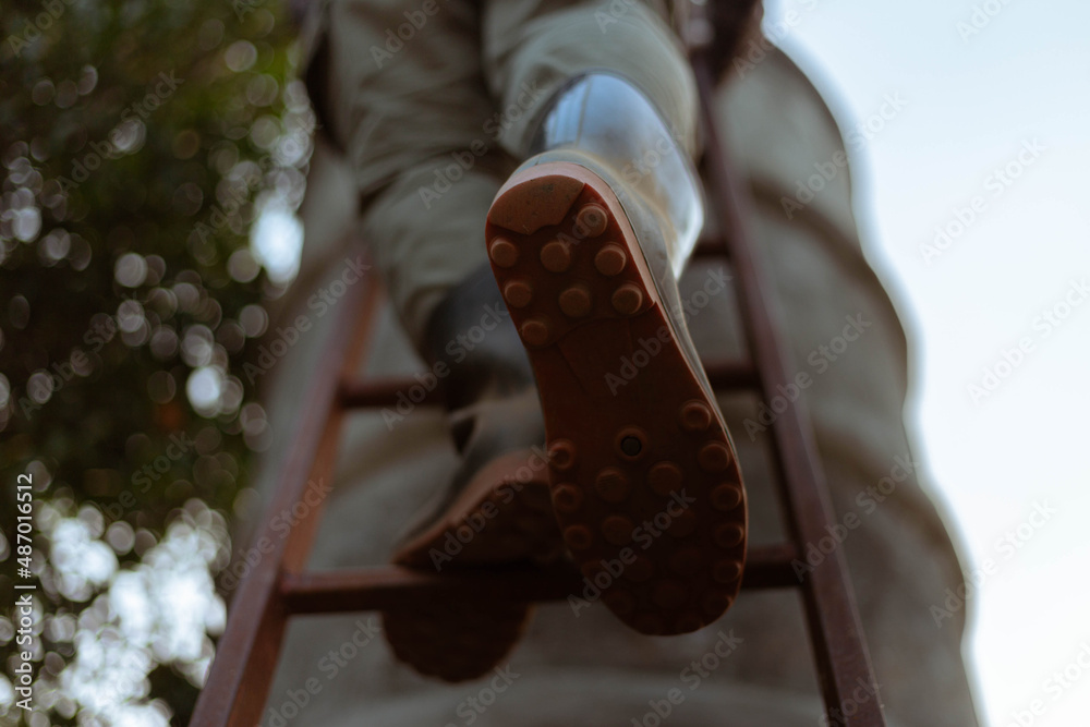 Gardening concept a male farmer wearing big boots climbing on a wooden ...