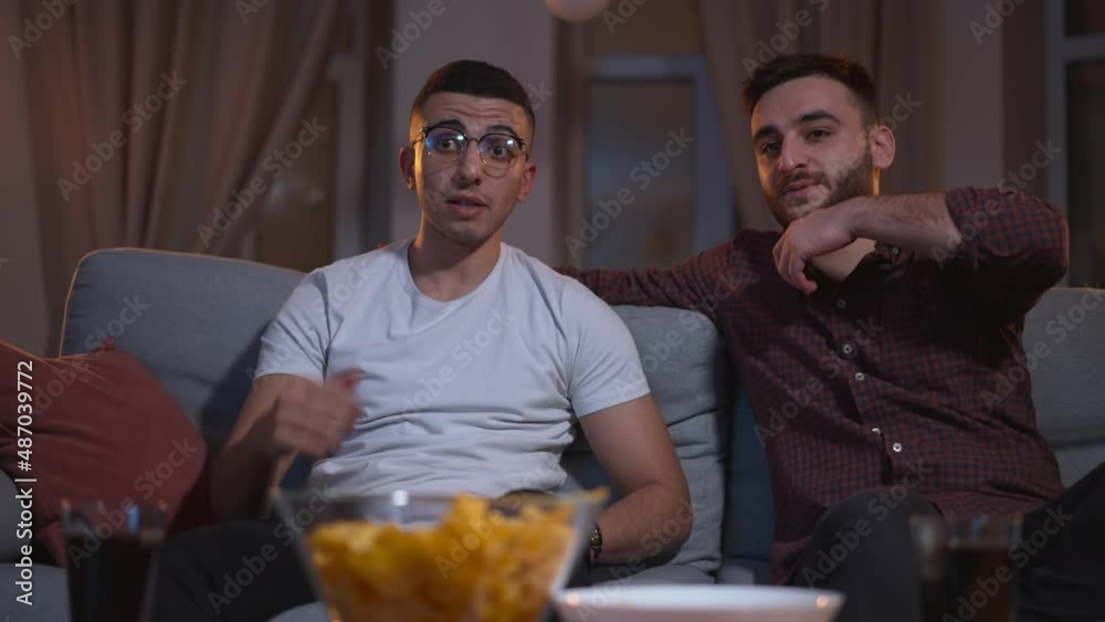 Male fans watching football and talking while sitting on sofa in home ...