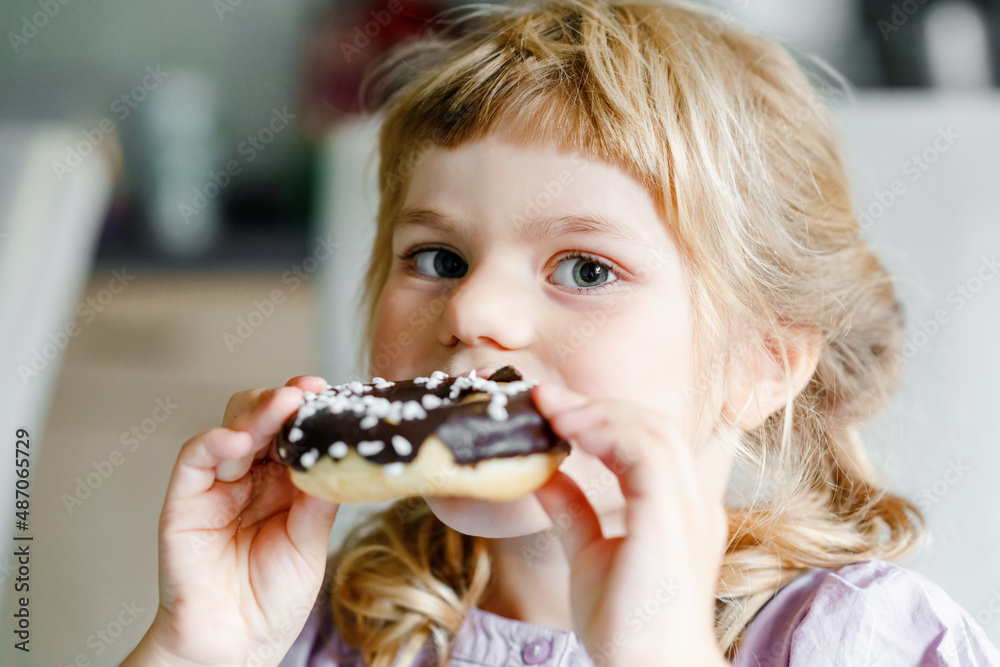 Happy little preschool girl eating sweet donut indoor. Blond child in ...
