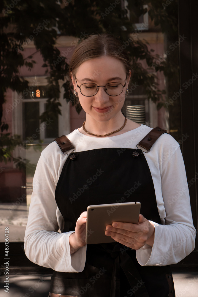 Waitress stands outdoors in summer with a tablet in her hands near the ...