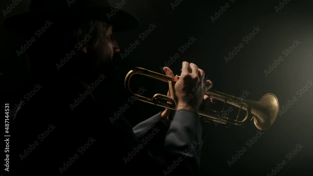 Man in tuxedo performs on stage in spotlight playing music on trumpet ...
