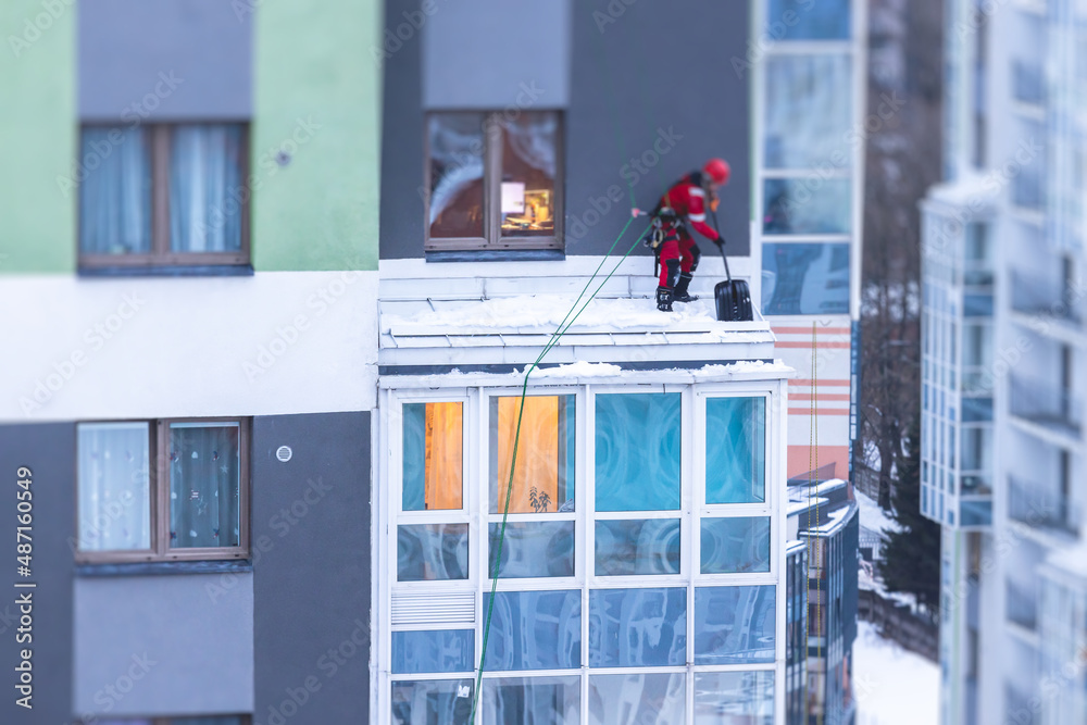 Professional climber rope access worker with a shovel removes snow and ...