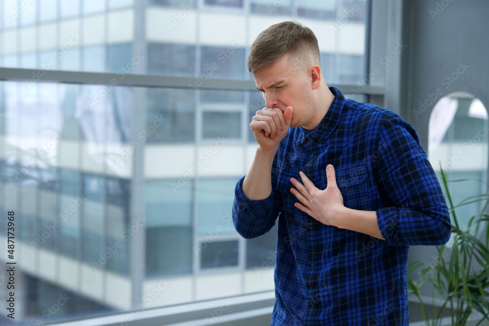 Sick ill guy, young man worker at job, work is coughing in his fist ...
