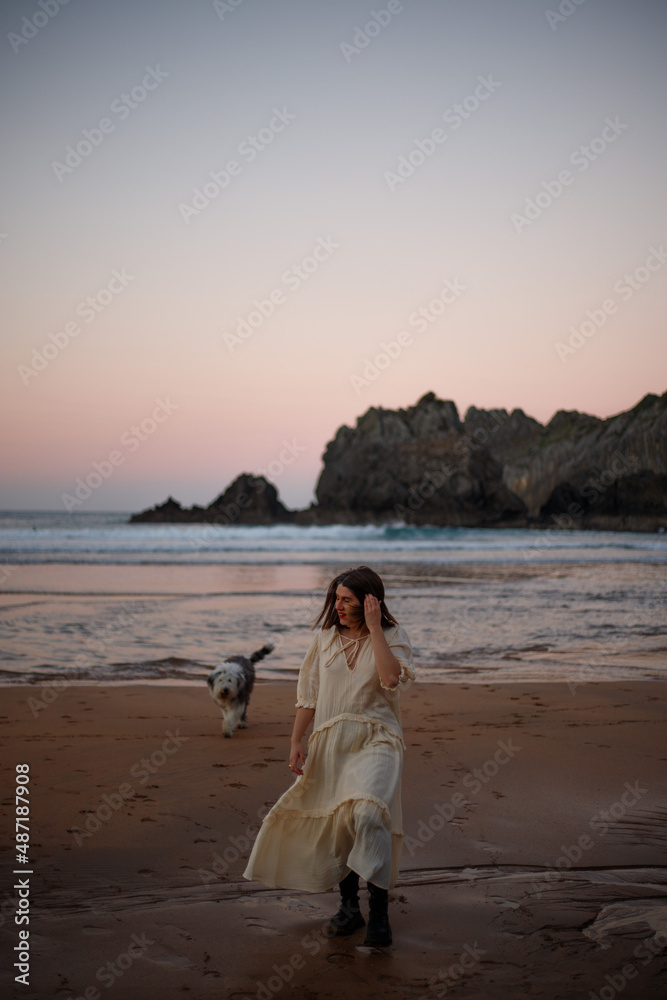 young girl enjoying the sunset with her dog on the beach in a long ...
