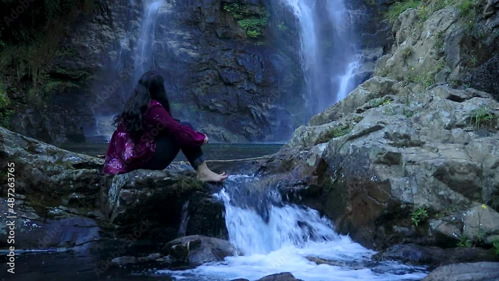 Vidéo Stock girl sitting on rock with waterfall flowing water from ...