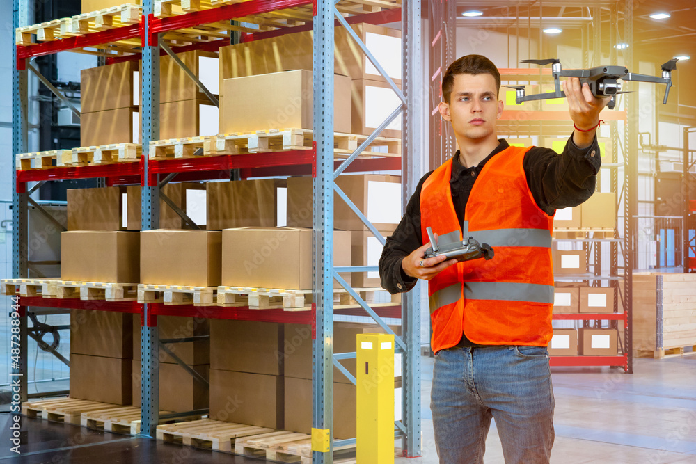 Young warehouse worker with quadcopter. Man launches drone in warehouse ...