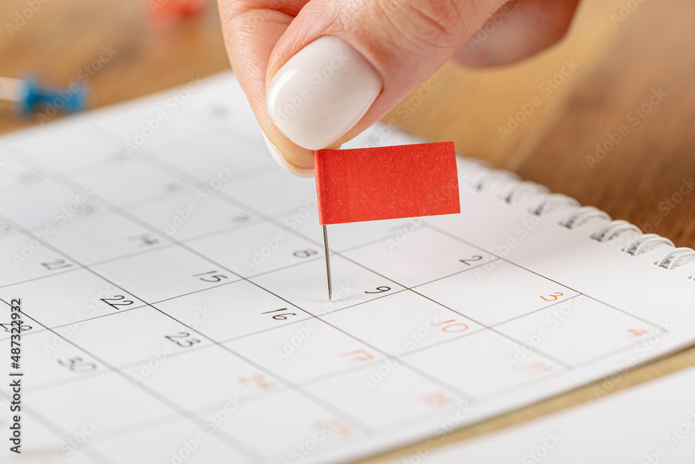 Hands fixing notes schedule, red flag pin thumbnail in 9 day calendar ...