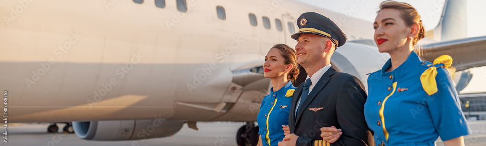 Excited male pilot walking together with two flight attendants in blue ...