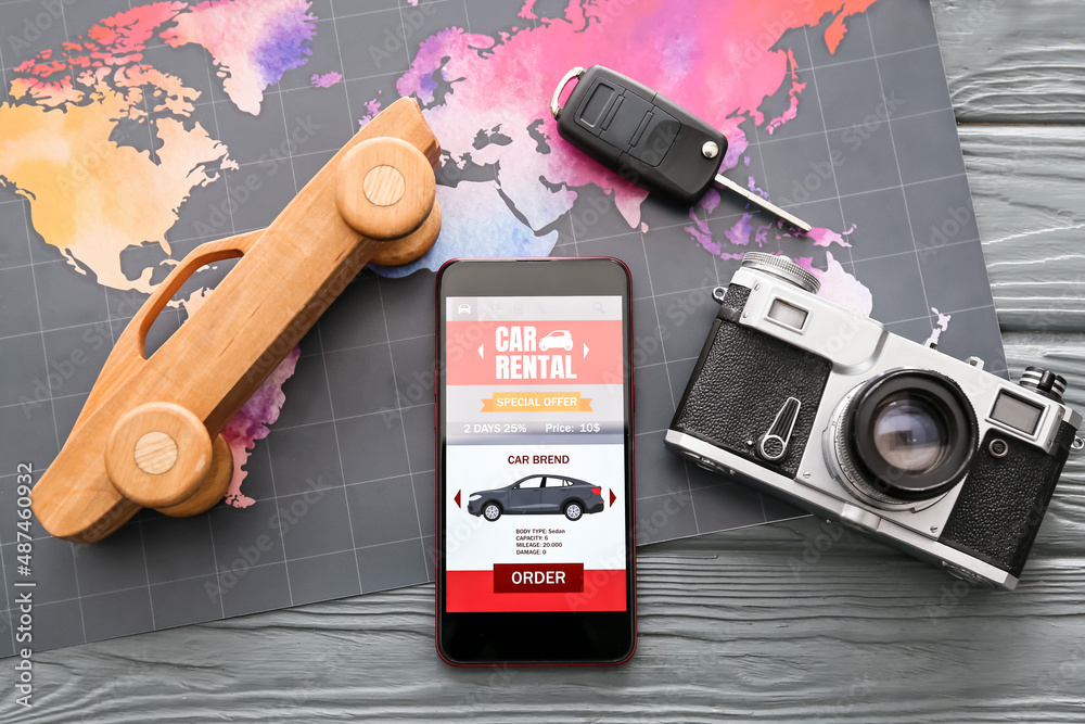 Mobile phone with open car rent app, toy, photo camera and map on dark ...