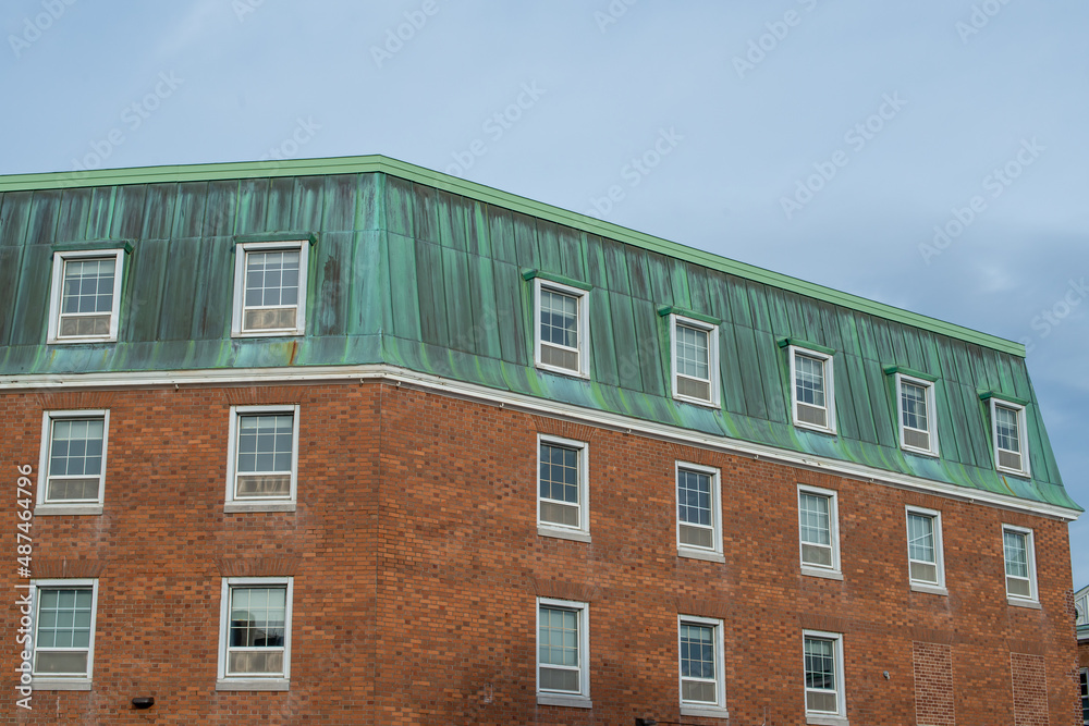 The corner view of a vintage brick building with a copper hip roof that ...