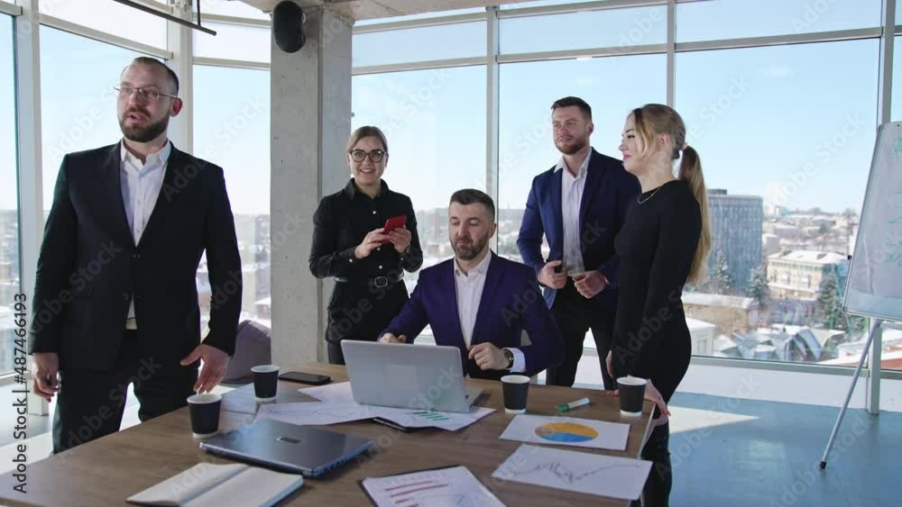 Business chief sits at the desk in front of laptop. Office team gathers ...
