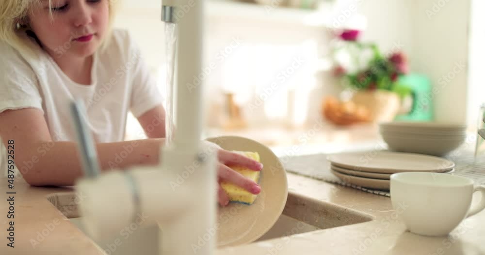 young boy washes the spoons and plates under the tap water, house ...