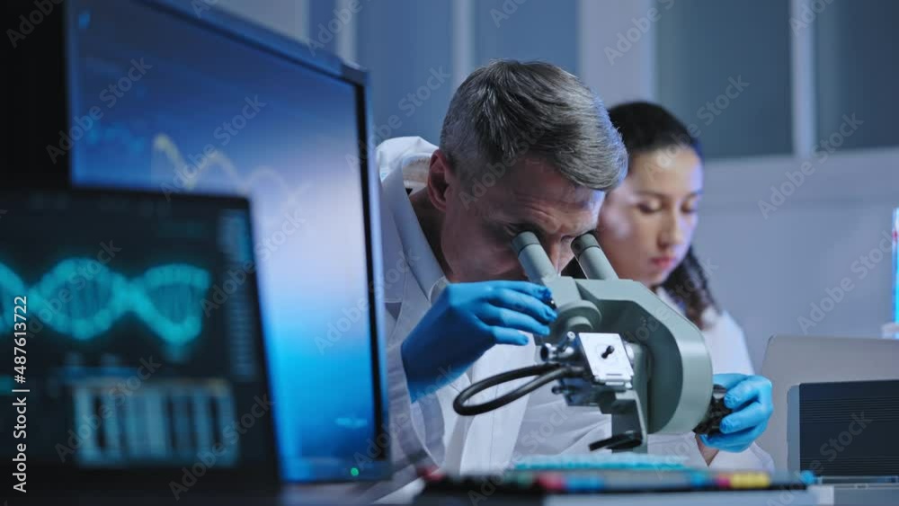 Experienced laboratory scientist looking in microscope, working on DNA ...