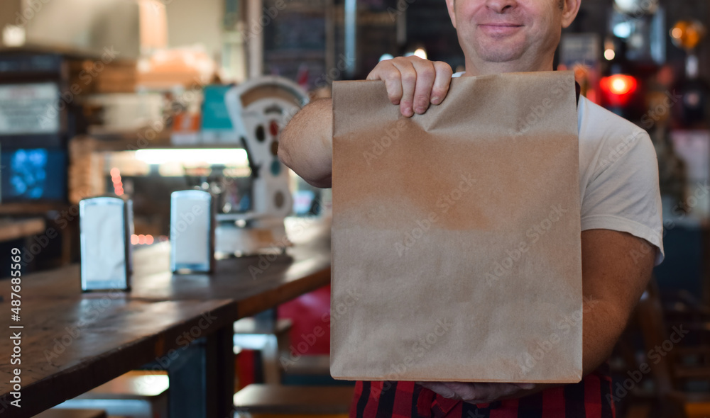 Restaurant employee holding paper take out bag with customer food order ...