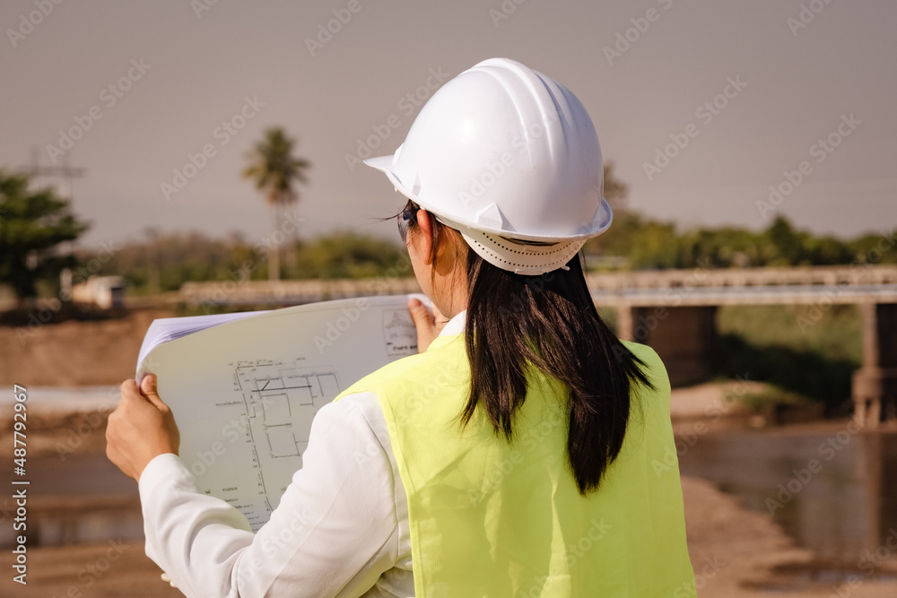 Asian female engineer wearing a helmet and safety vest works and looks ...
