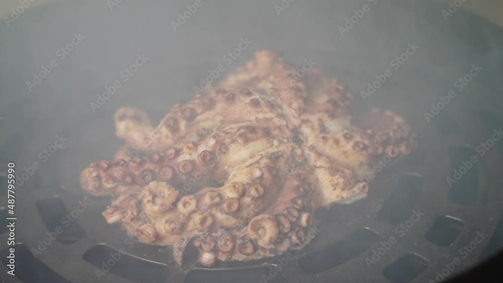 Aromatic smoky smoked octopus cooking slowly on an open flame barbeque ...