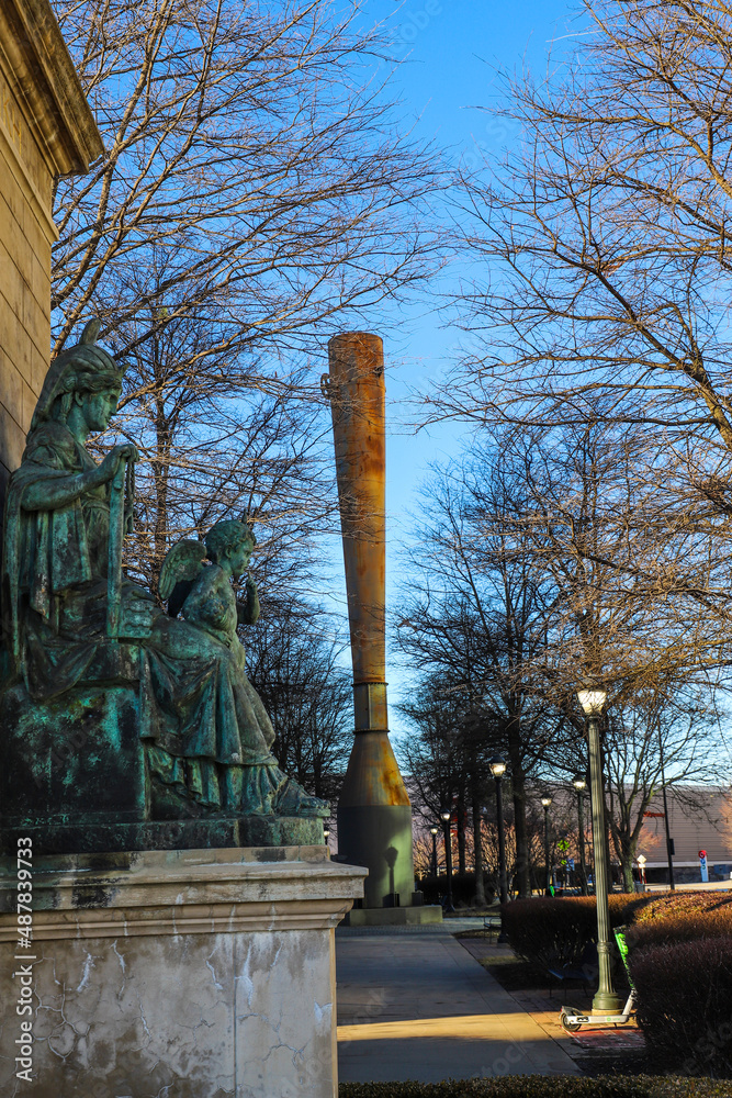 a statue of a woman and a child in the park with a tall rusty smoke ...