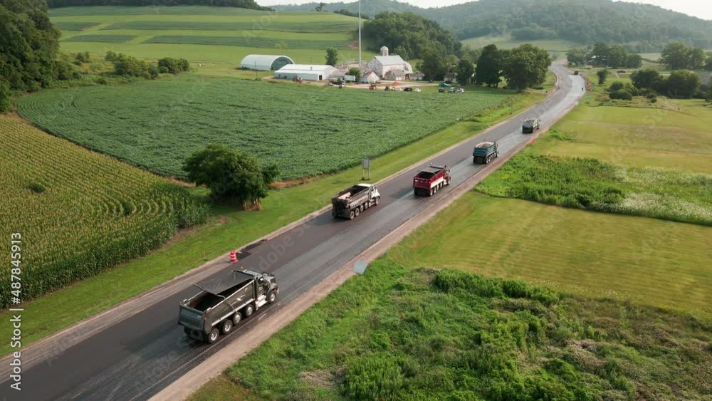 Road construction crew working with dump trucks along a rural highway ...