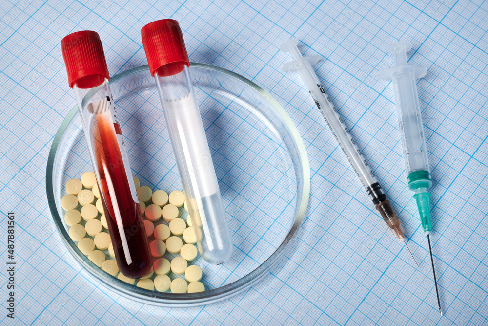 Blood test-tubes, injection syringes, pharmacy capsules in a Petri dish ...