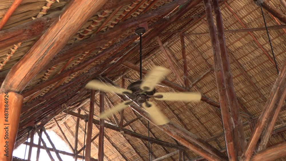 Big fan hanging from the ceiling spinning with a straw roof in the ...