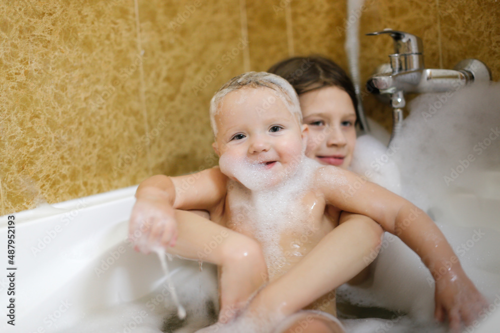 Cute sibling children bathe in a bubble bath together. Children in the bathroom. The concept of ...