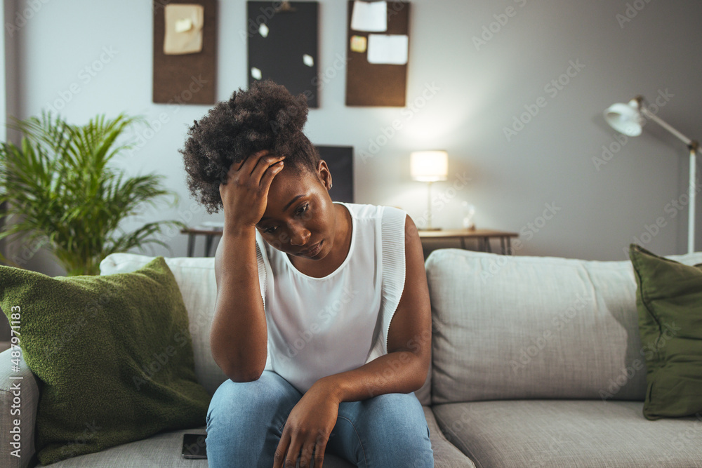 Young woman in gray clothes is sitting curled up on bed at home. Upset ...