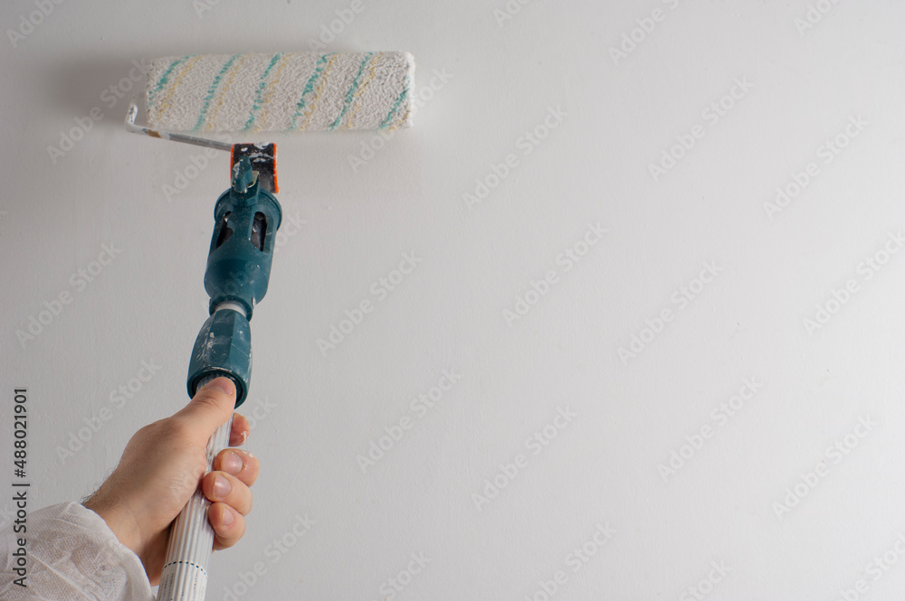 Detalle de mano y rodillo pintando en superficie blanca, espacio para ...
