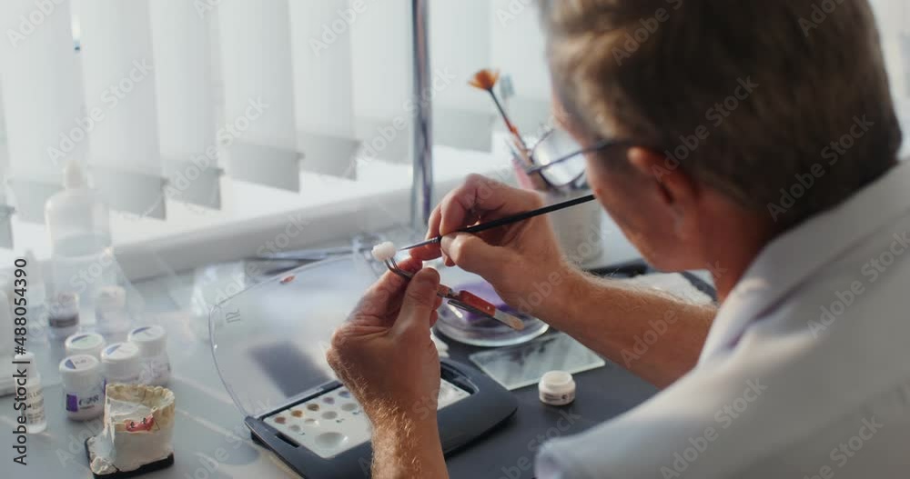 Close-up of painting a ceramic dental crown with a thin brush by hand ...