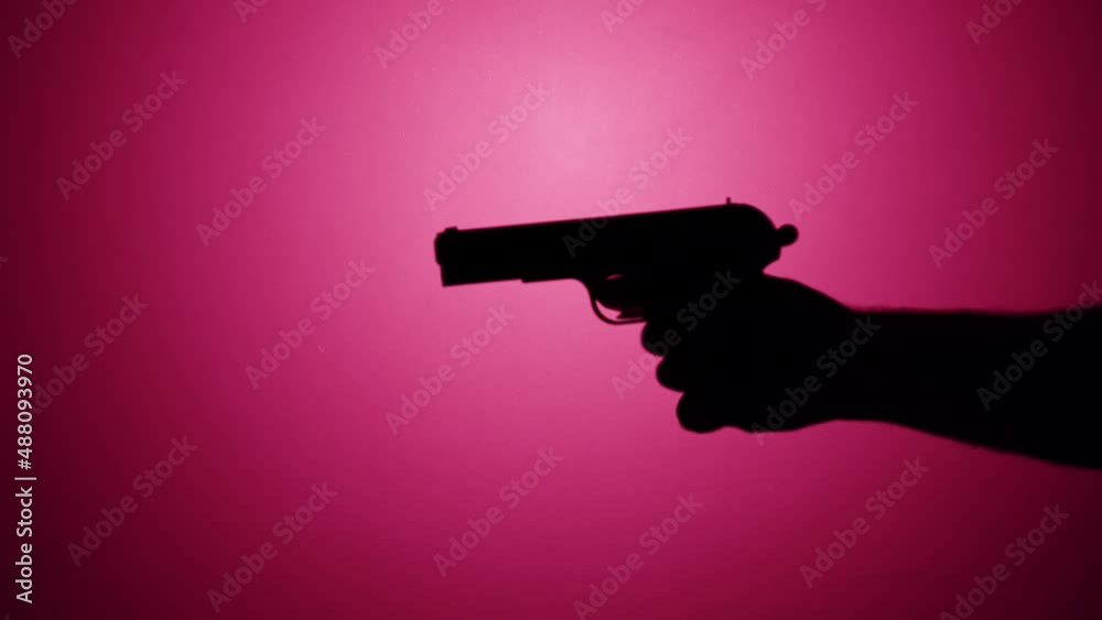 Man holding gun close-up, shadow silhouette of hand with pistol on pink ...