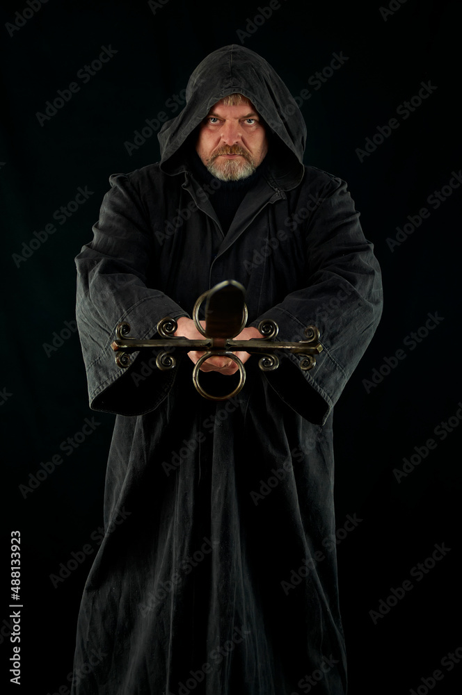 Portrait of courageous monk-warrior in black cloak with sword in hands ...
