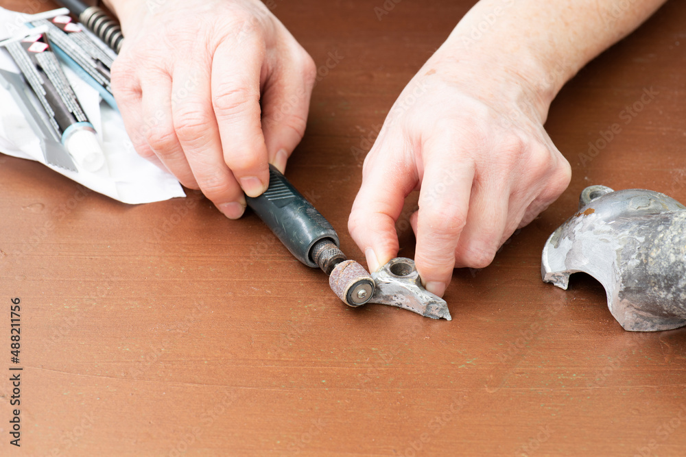 Manos con una lijadora, lijando una pieza rota de metal para unirla con ...