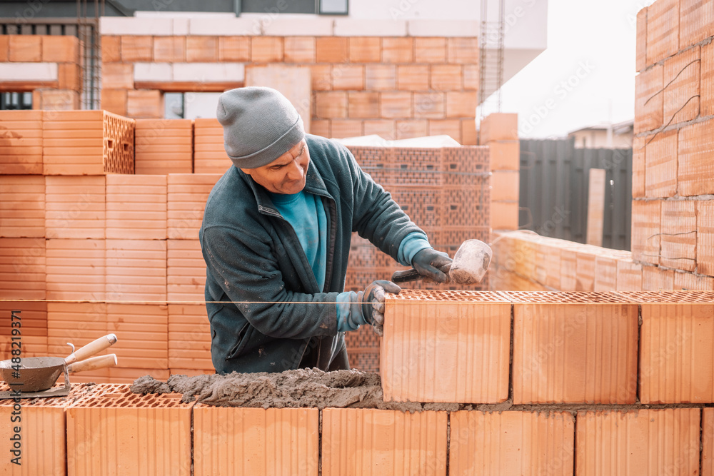 Bricklayer industrial worker installing brick masonry on exterior wall ...