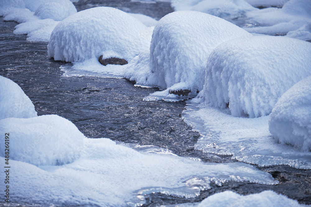 Stones with snow caps and ice in the water of frozen river in winter ...